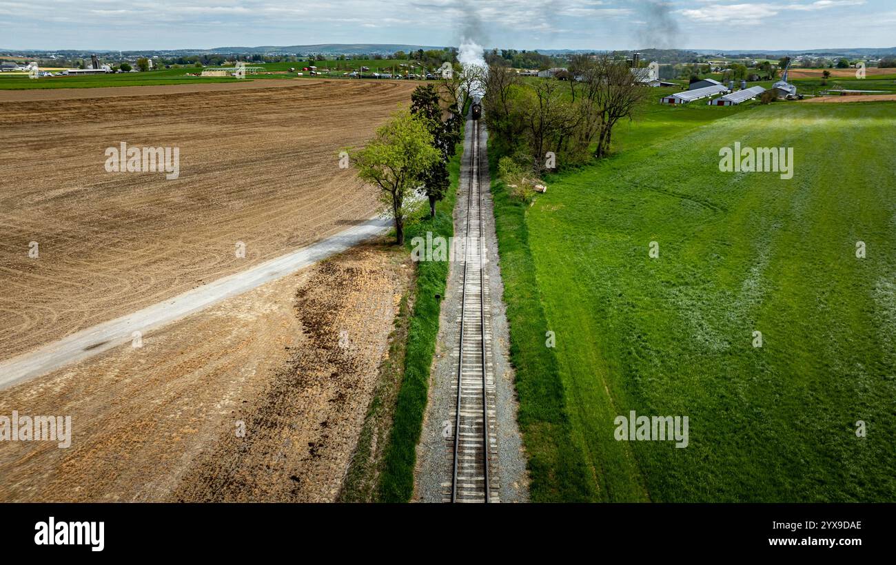 A peaceful rural landscape shows railway tracks stretching through fields of green grass and ...