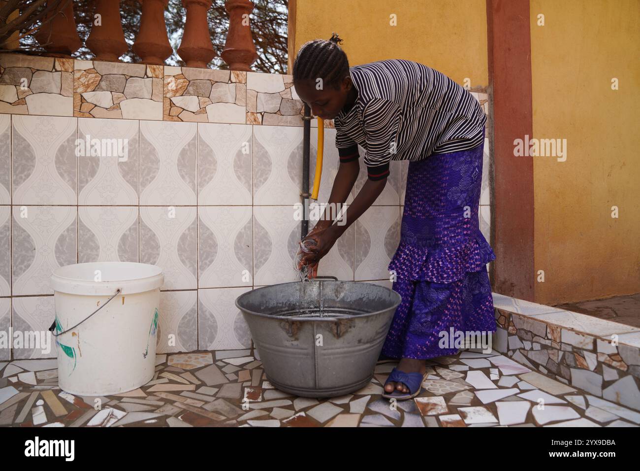 Side view of a young African village girl washing dishes at the public ...