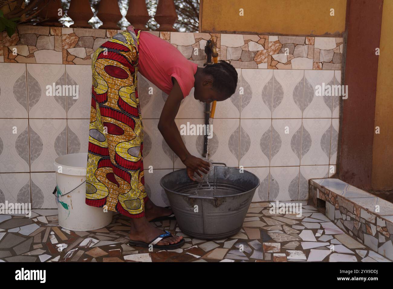 Adolescent African girl cleaning dishes at a tidy washing area with ...