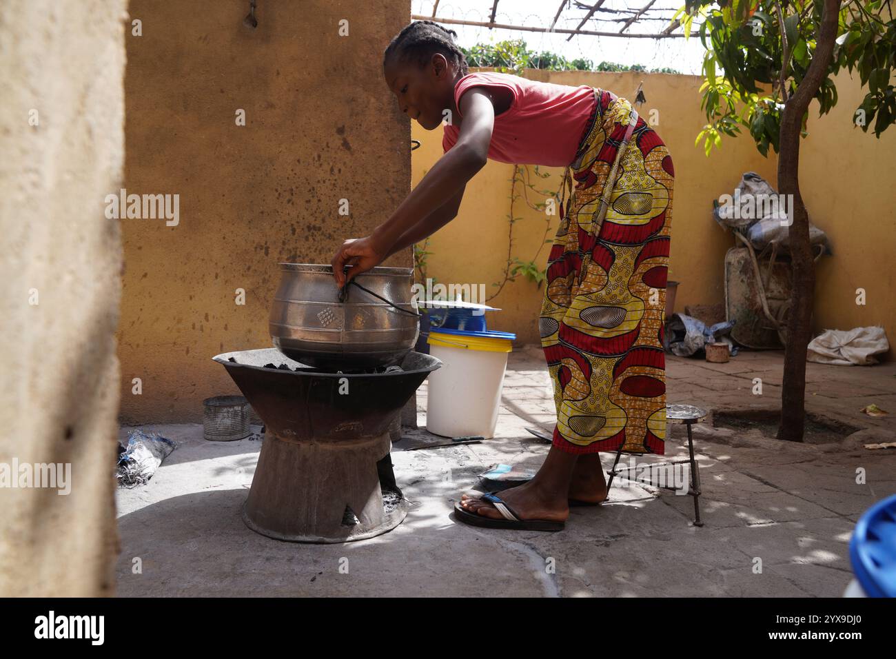Young African girl operating a giant pot while cooking her family's ...