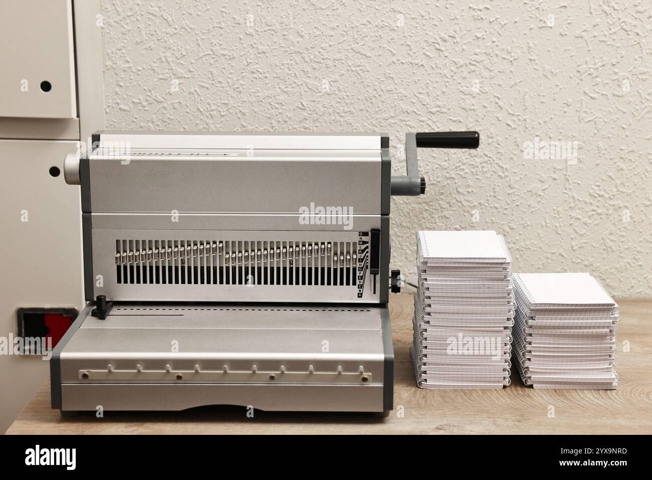 Modern binding machine and stacks of notebooks on wooden table indoors ...