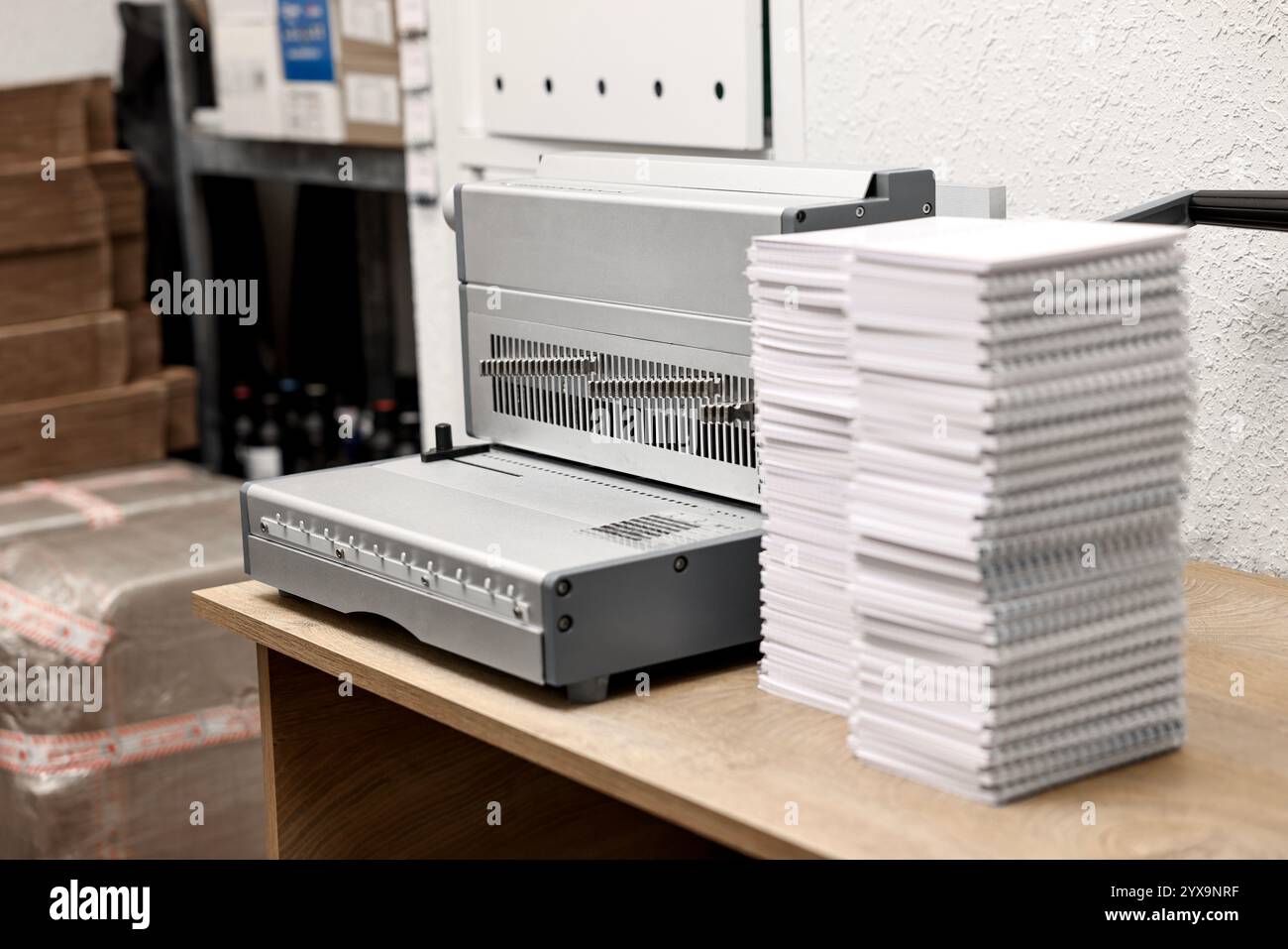 Modern binding machine and stacks of notebooks on wooden table indoors ...
