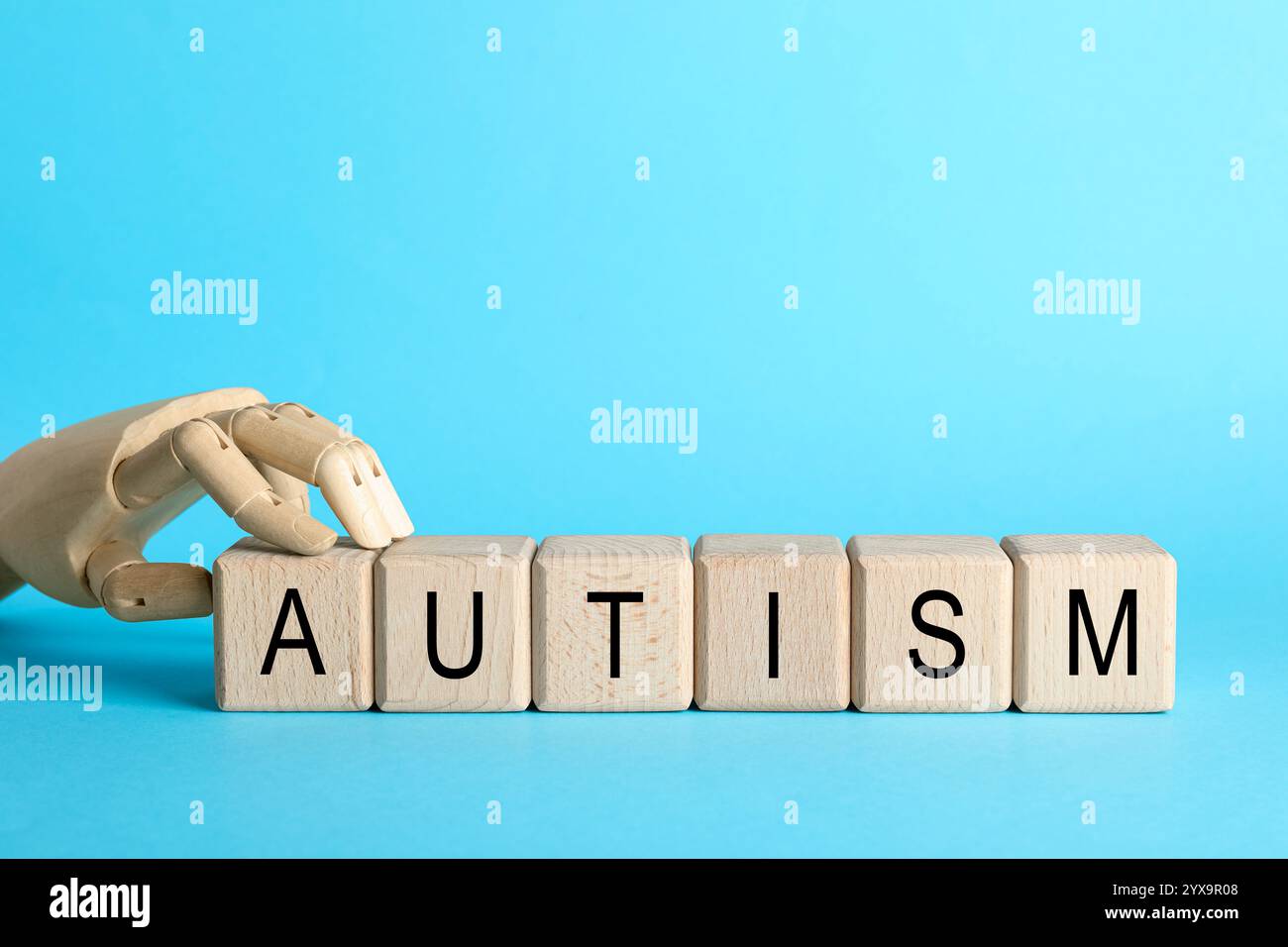 Word Autism made of wooden cubes and mannequin hand on light blue ...