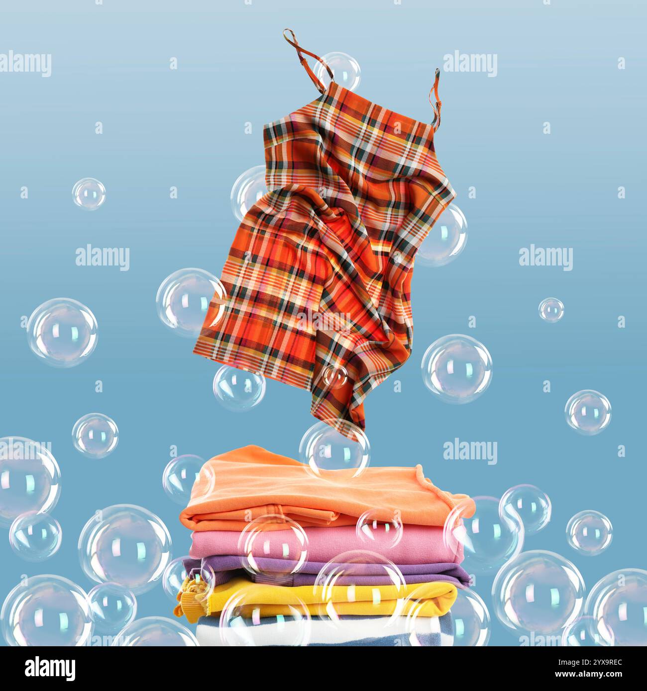 Stacked laundry and flying dress among floating soap bubbles on light ...