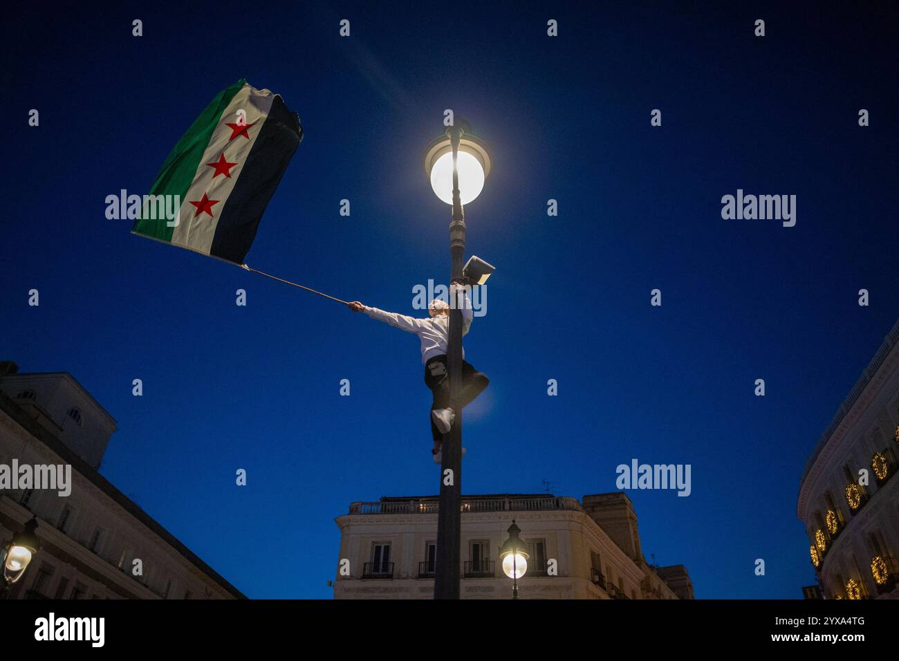 A protester stands on a lamppost raising a Syrian flag during a rally ...