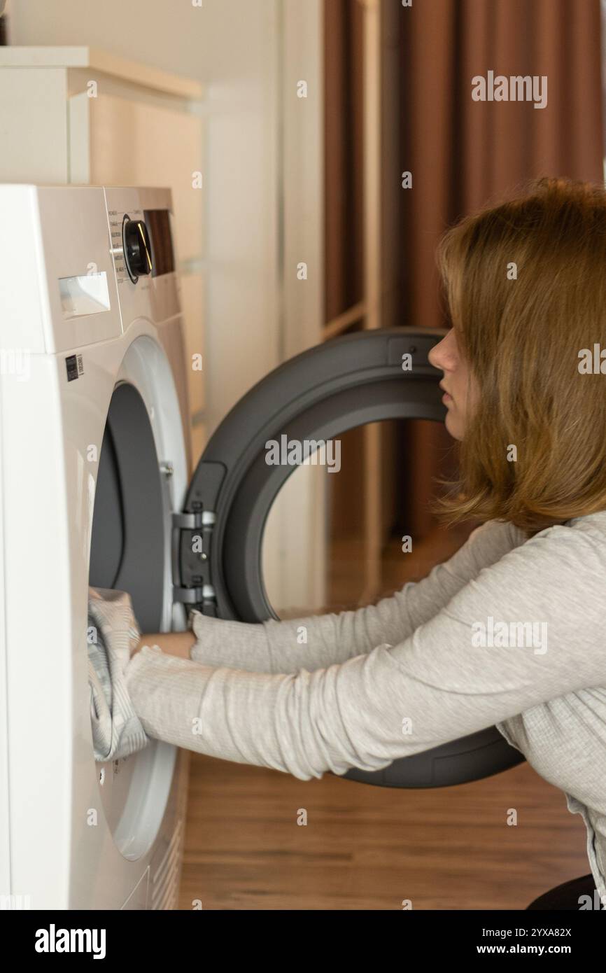 A woman is placing clothes into a front-loading washing machine in a ...