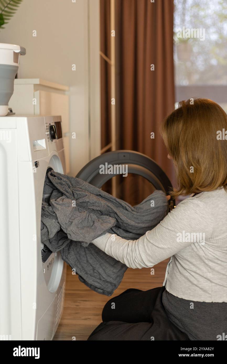 A woman is kneeling on the floor as she carefully loads a large gray ...