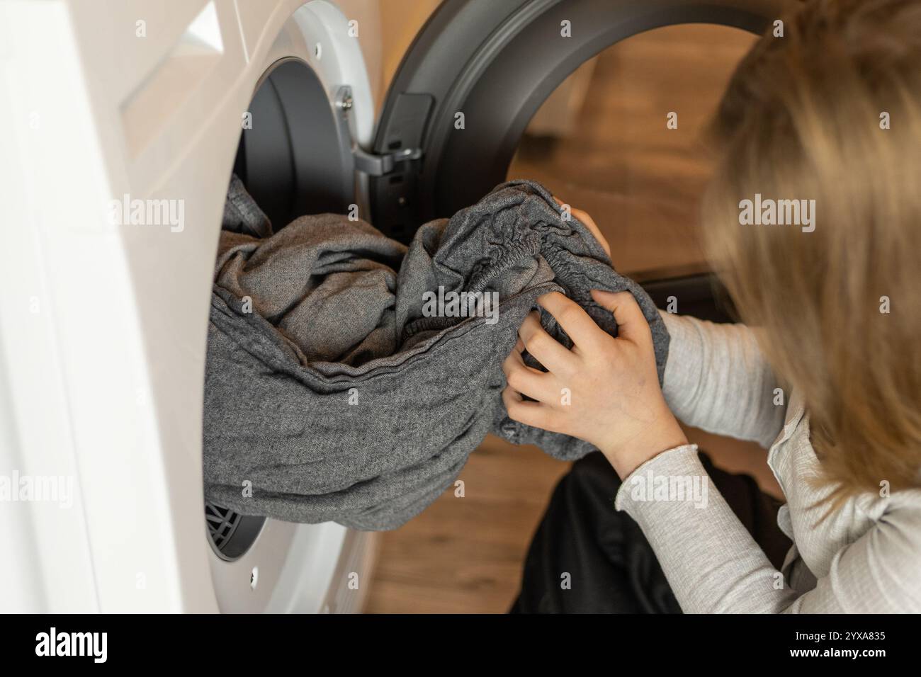 A person is loading a gray garment into a front-loading dryer in a cozy ...