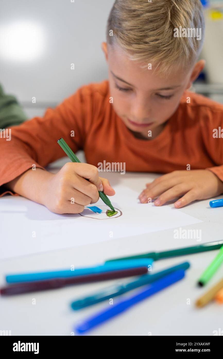 Elementary school student focused on drawing with colorful markers ...