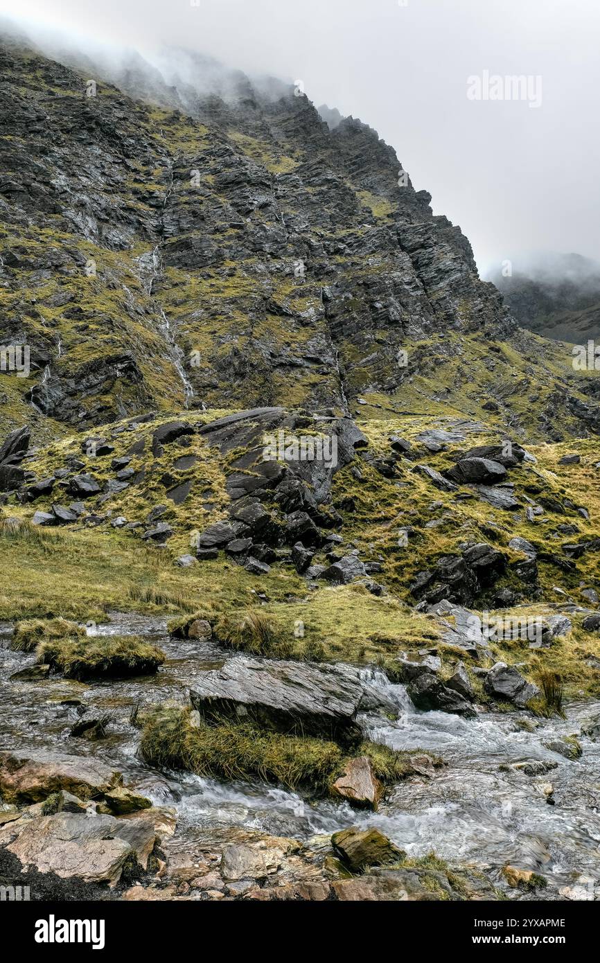 A rugged hillside rises steeply with patches of grass and rocks, while ...