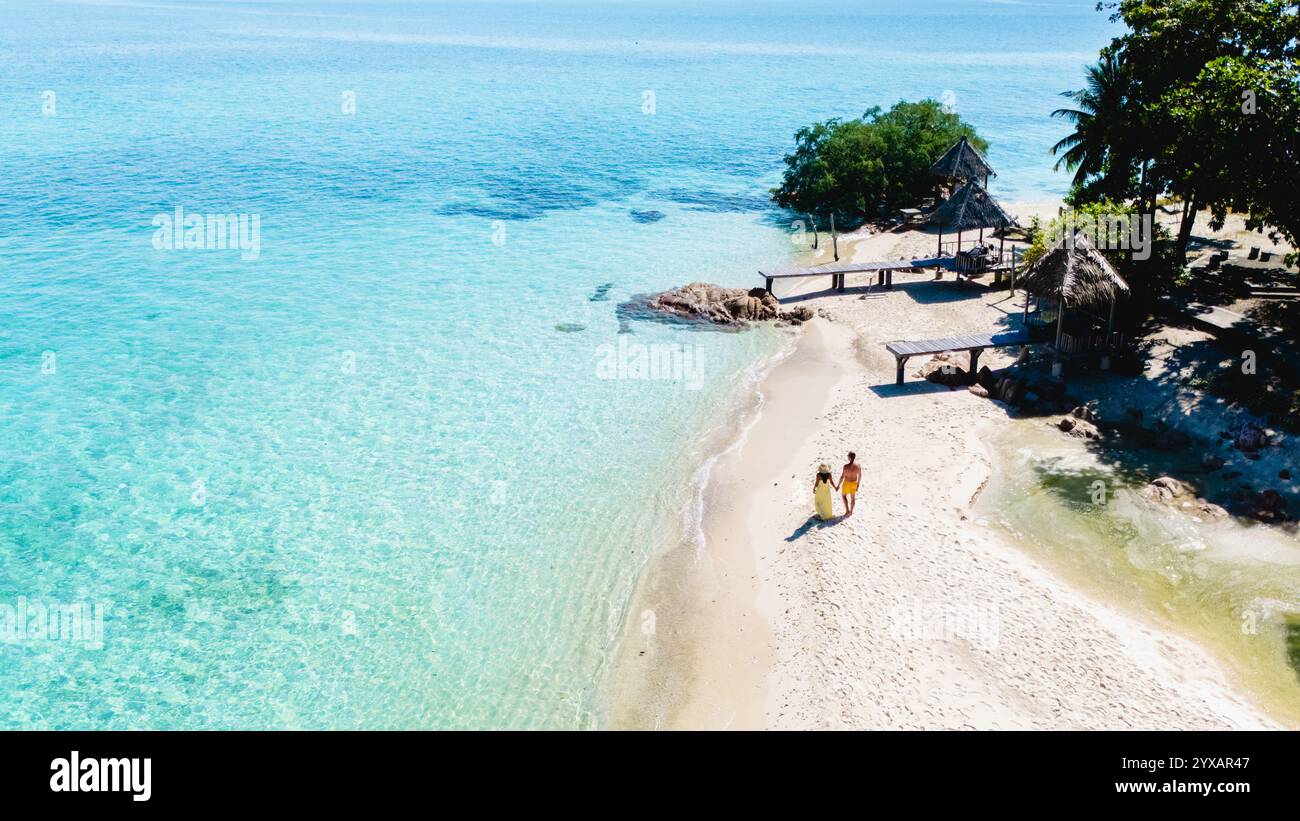 Warm sunlight illuminates the pristine beach as two people stroll along ...