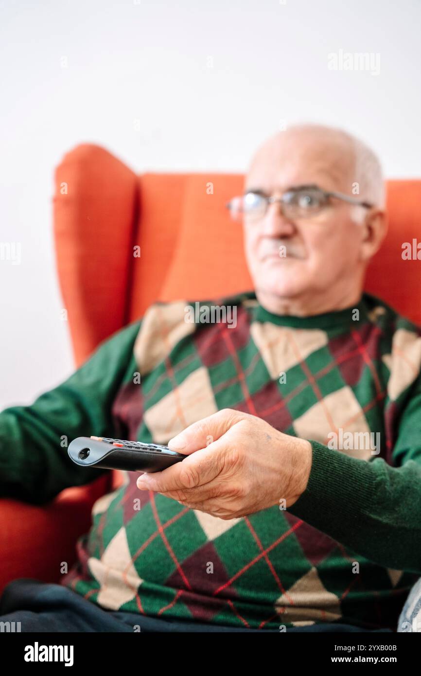 Elderly man holding TV remote control at home. Grandfather watching TV ...