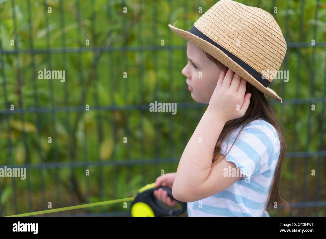 Little girl in a straw hat walking a small dog in the summer on a leash ...