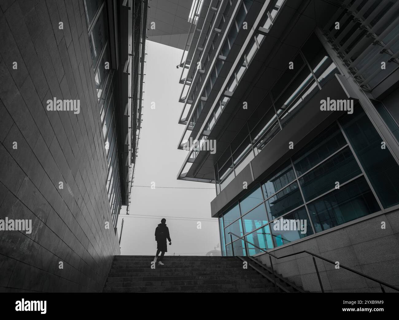 A man in dark clothing walks up stairs between two modern glass ...