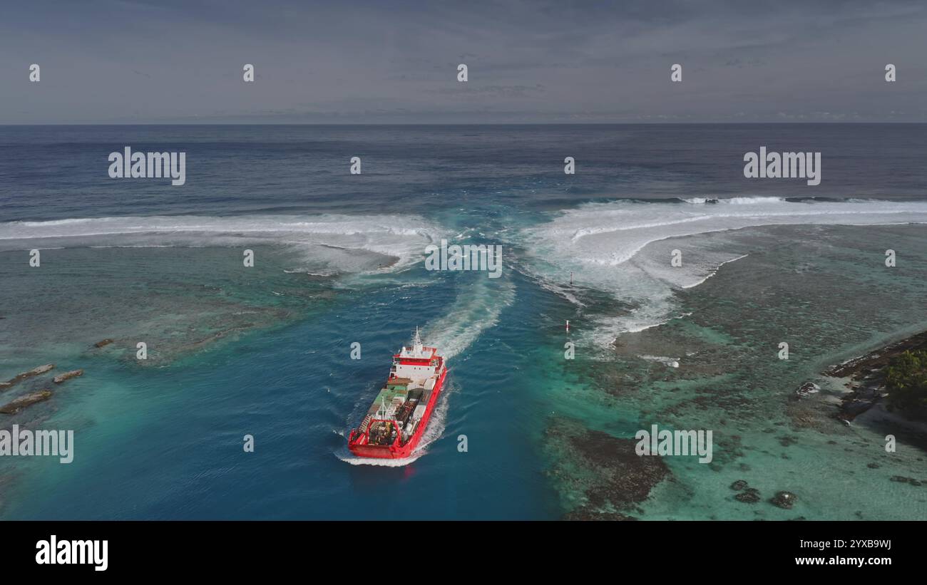 Aerial view of red cargo ship navigating ocean channel between coral ...
