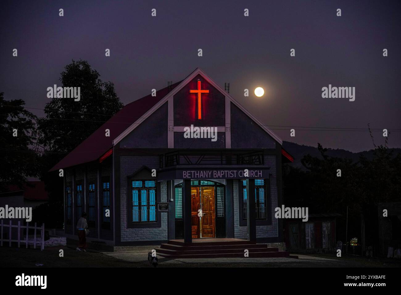 A Kuki tribal woman walks past a church as the full moon rises ahead of ...