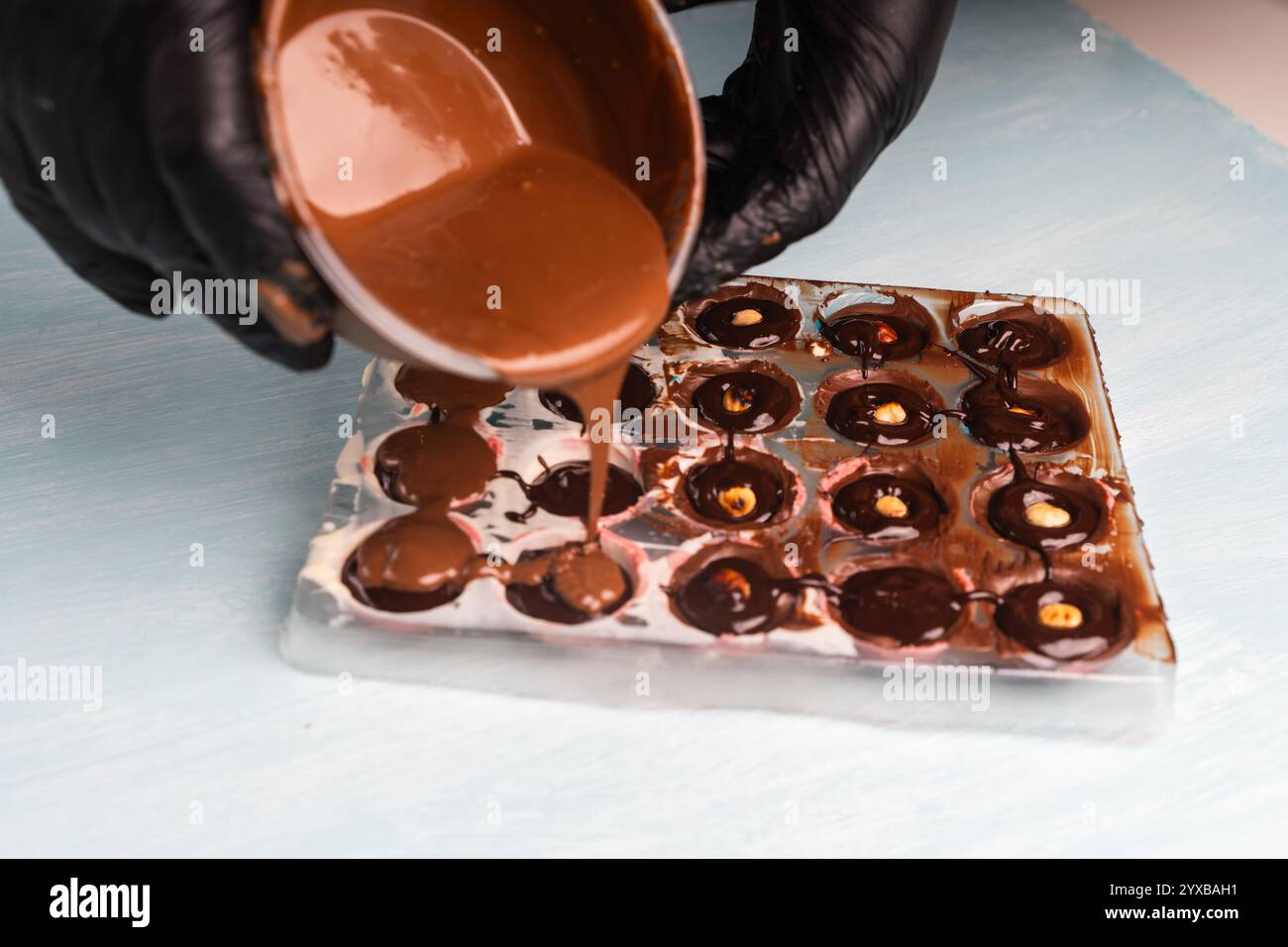 The chef's hands pour tempered chocolate into a candy mold. The process ...