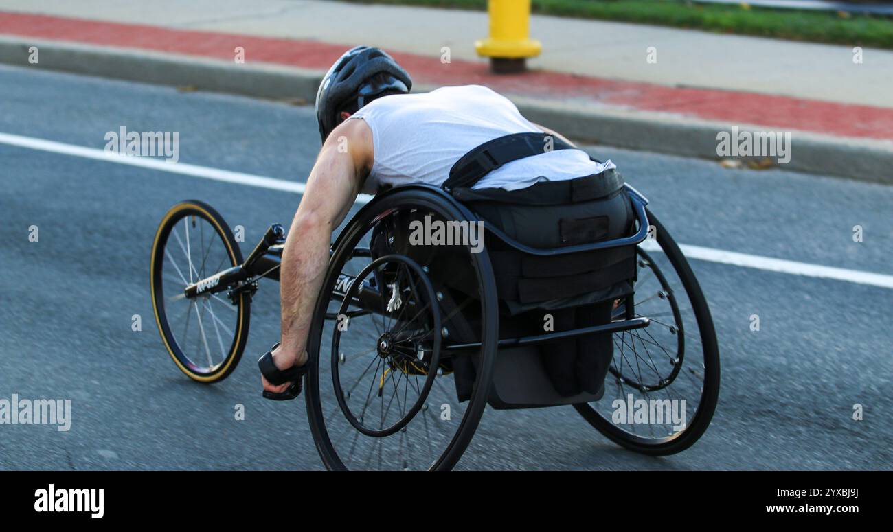 A determined athlete in a racing wheelchair propels forward on an urban ...