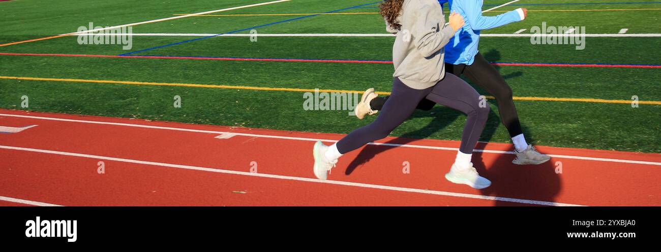 Two athletes run side by side on a red track on a clear afternoon ...
