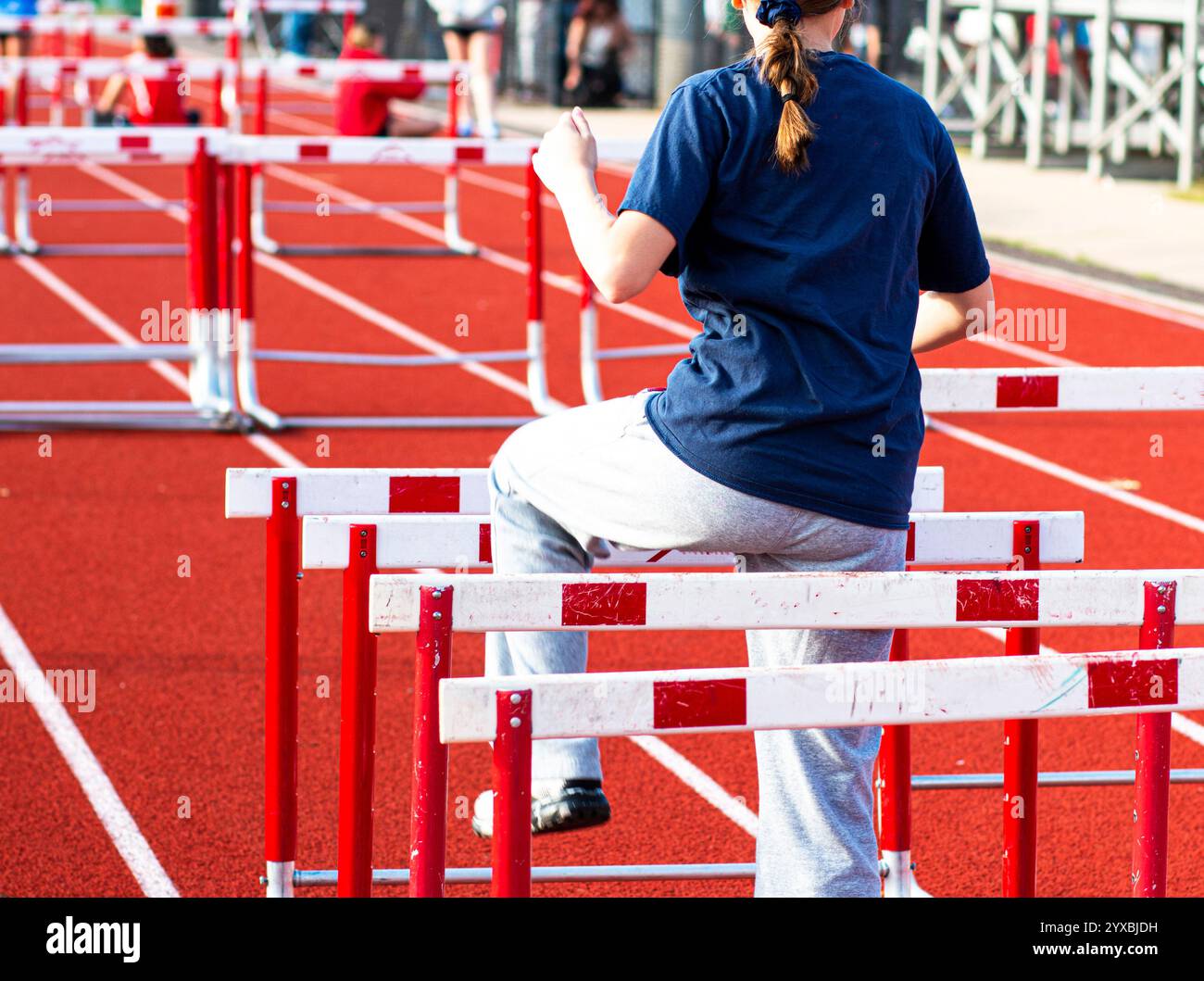 An athlete in training navigates hurdle barriers on a track, displaying ...