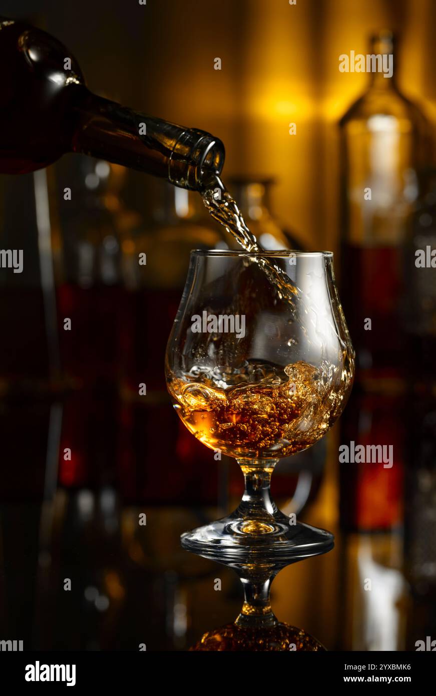 Pouring brandy from a bottle into a glass. Snifter of brandy on a black ...