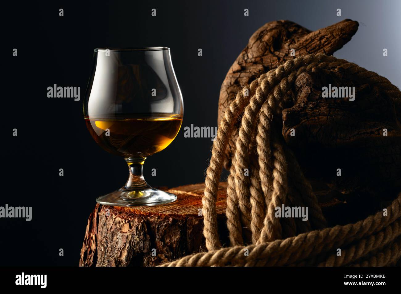 Brandy snifter and rope on a old stumb. Glass with whiskey, cognac or ...