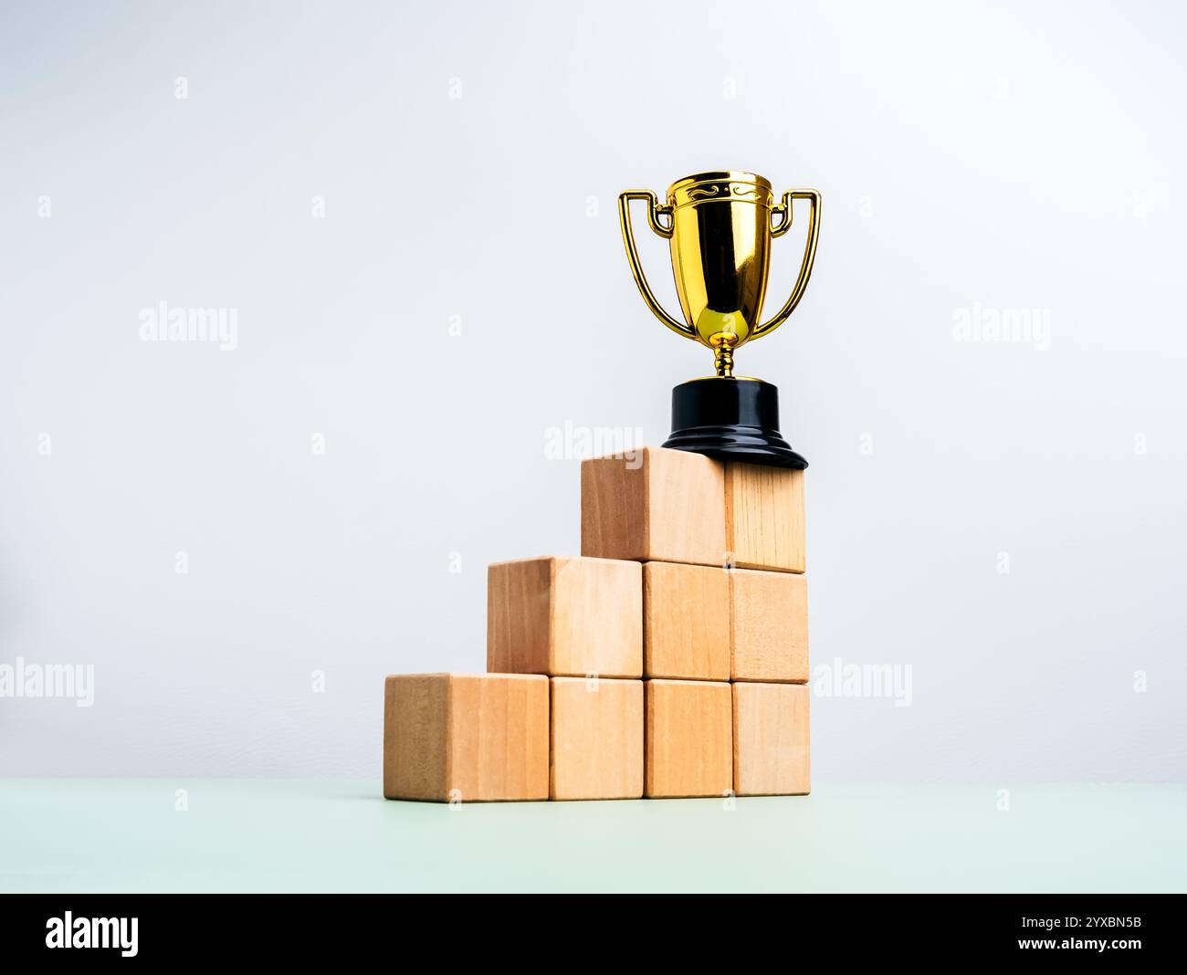 Gold trophy on top of wood cubes as bar graph chart steps on green and ...