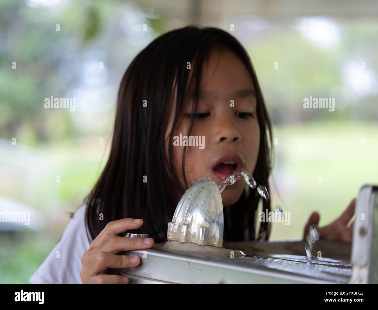 Cute girl drinks water from square shiny metal drinking fountain in a ...