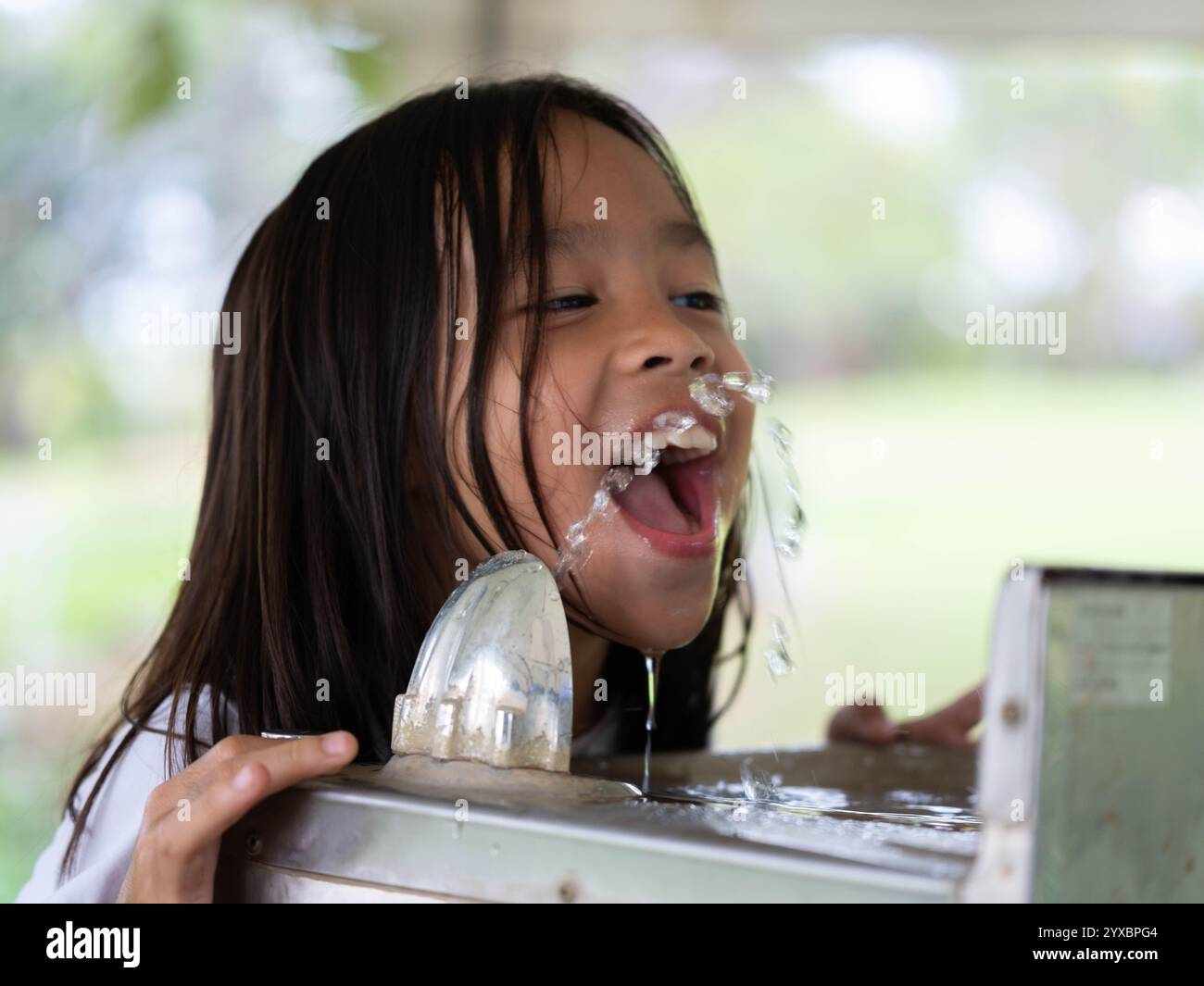 Cute girl drinks water from square shiny metal drinking fountain in a ...