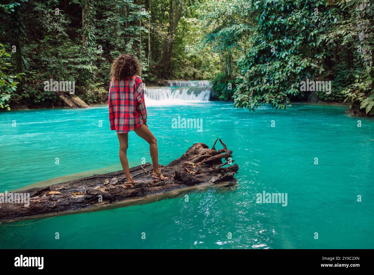 Woman in a plaid shirt standing on a log over a turquoise river in the ...