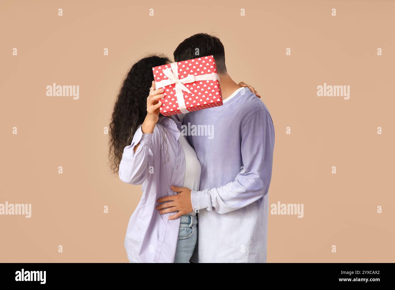 Loving young couple kissing behind gift box on beige background ...