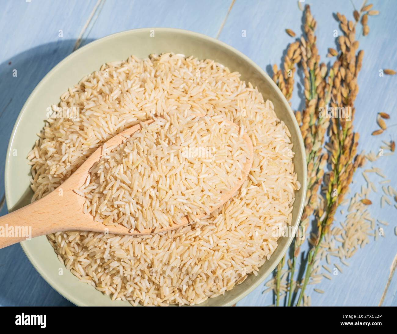 A bowl of brown rice is placed on a blue table next to a spoonful and ...