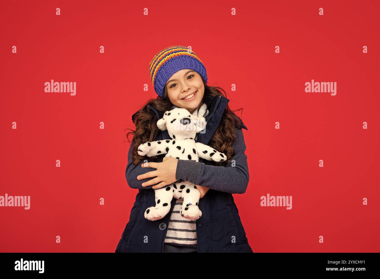 smiling child in puffer jacket hold toy. teen girl on red background ...
