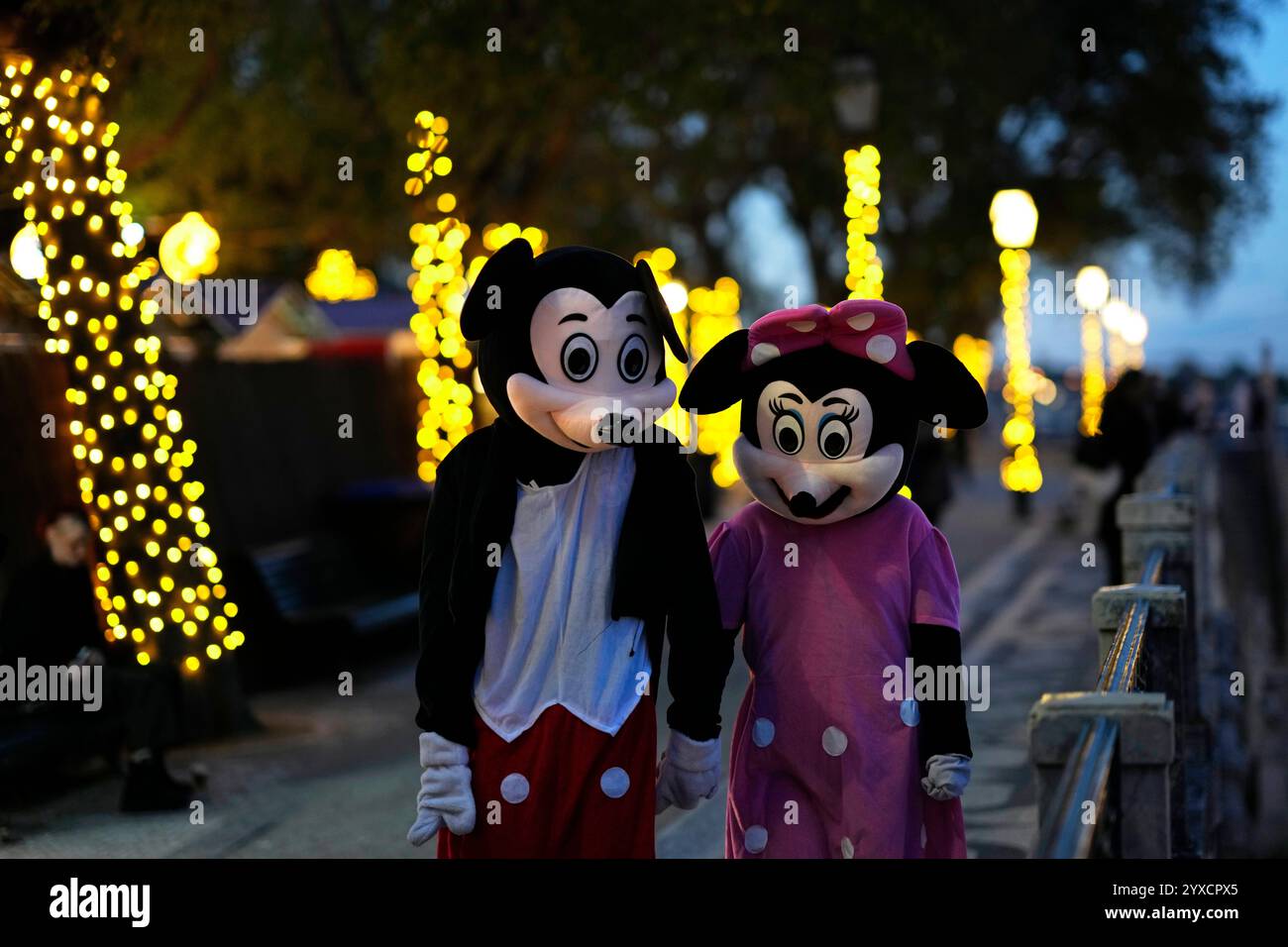 Two people wearing Mickey and Minnie Mouse costumes walk hand in hand ...