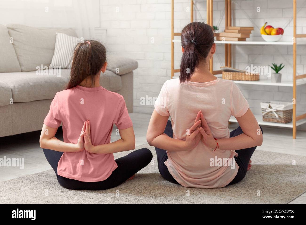 Back view of mother and daughter sitting in lotus pose, making namaste ...