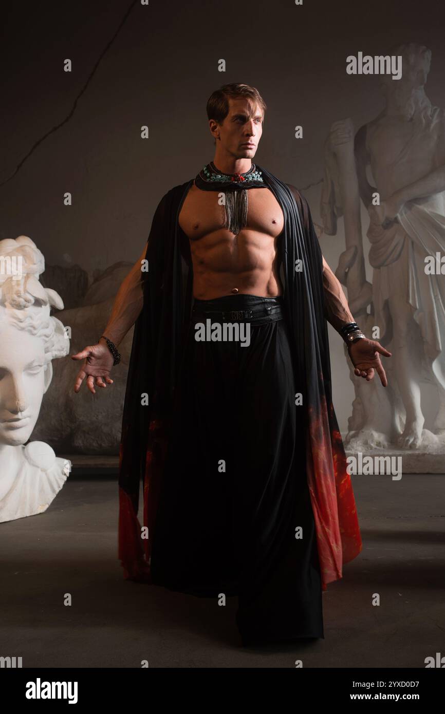 Muscular charismatic bodybuilder model in a silk cape makes an ...