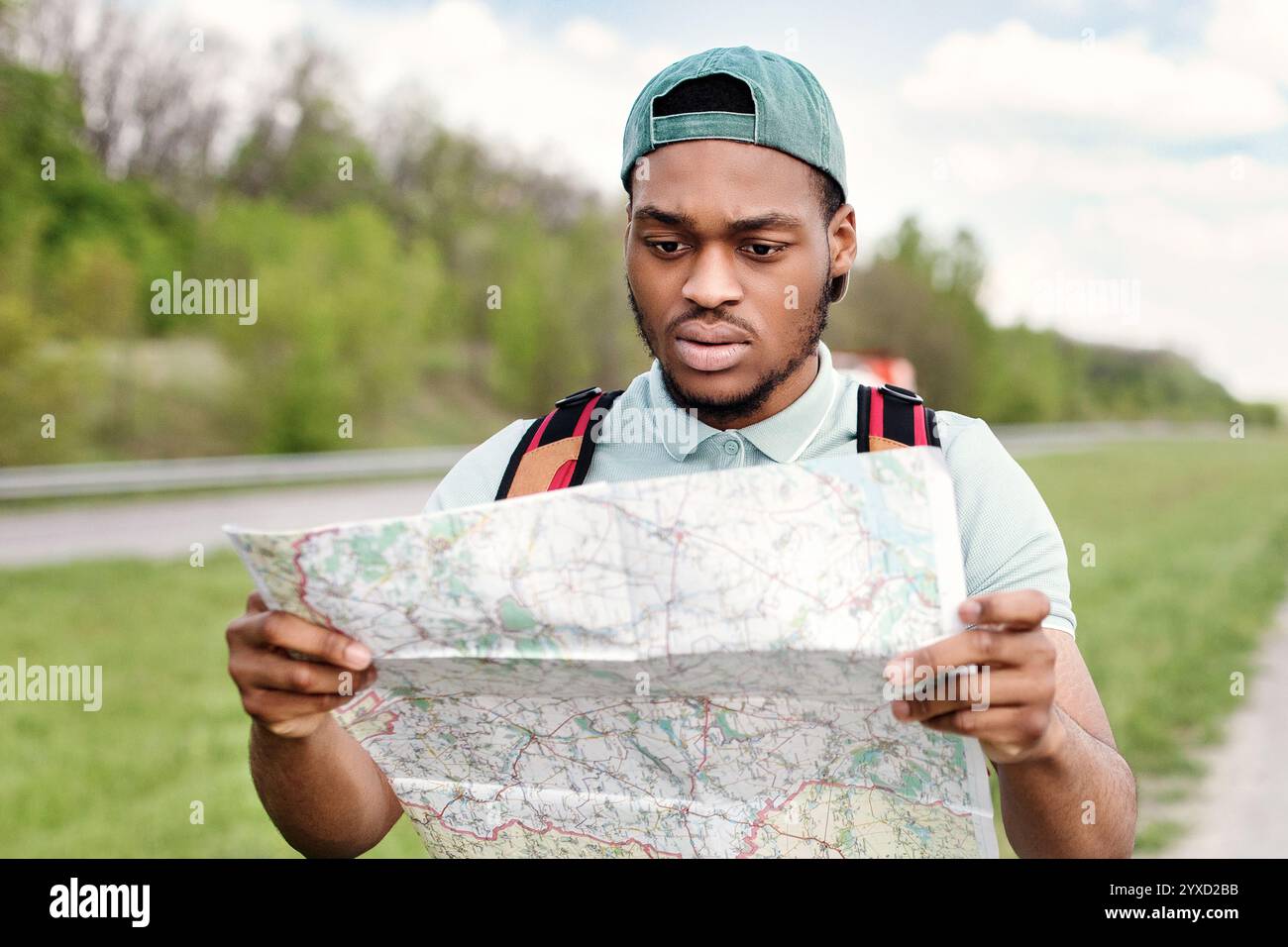 Unhappy young black man hitchhiking on road, looking at map, feeling ...