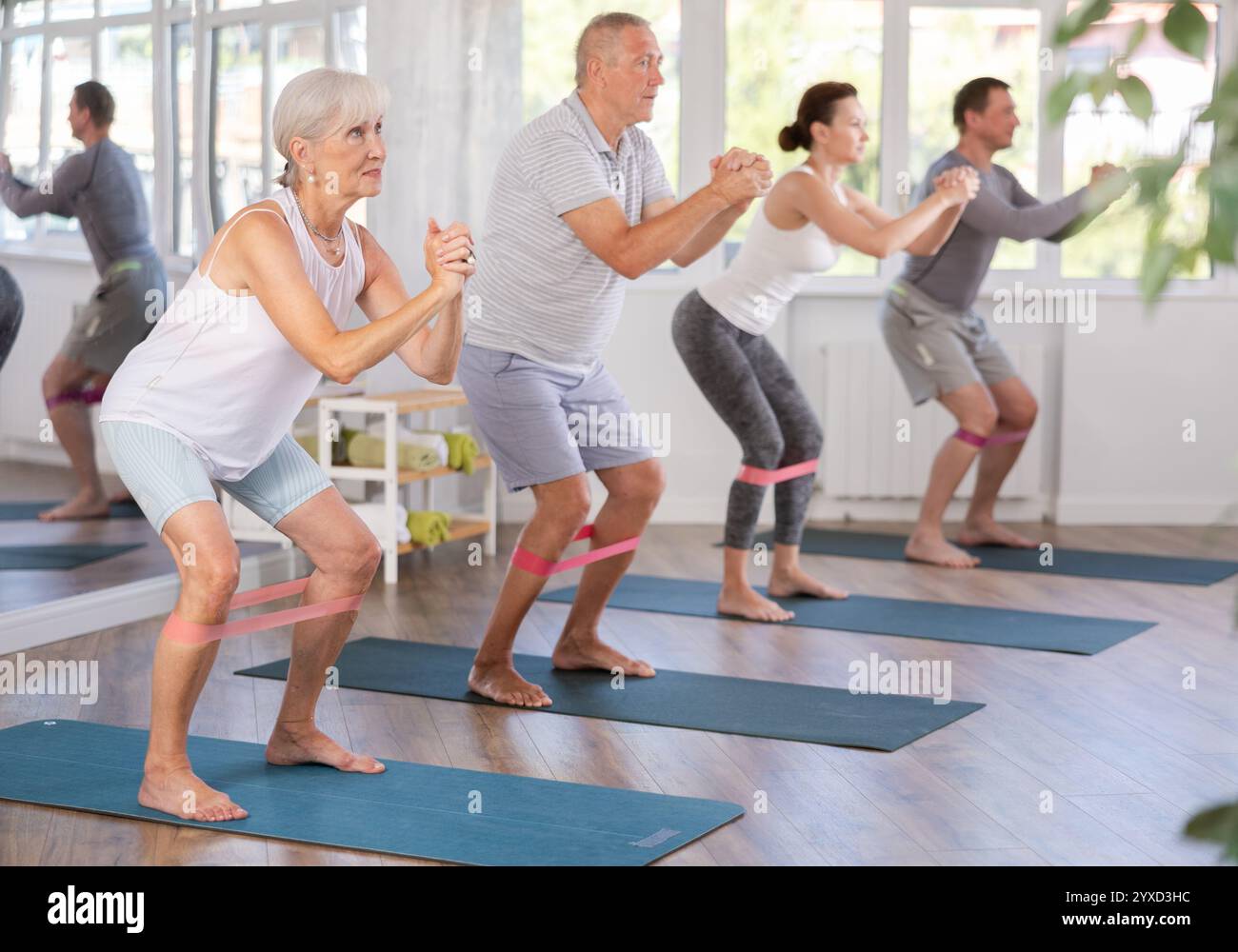 Elderly woman during Pilates strength training performs squats with ...