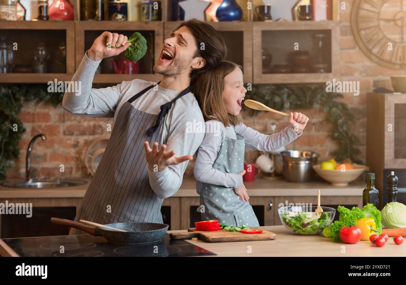 Kitchen Fun. Cheerful dad and his little daughter singing while cooking ...