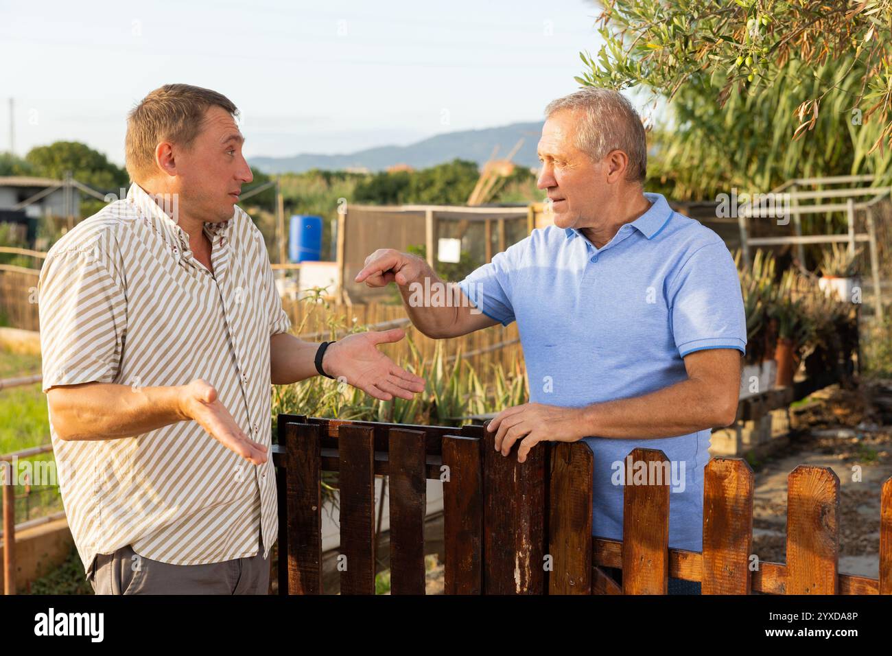 Dissatisfied men talking through wooden fence of country house on ...