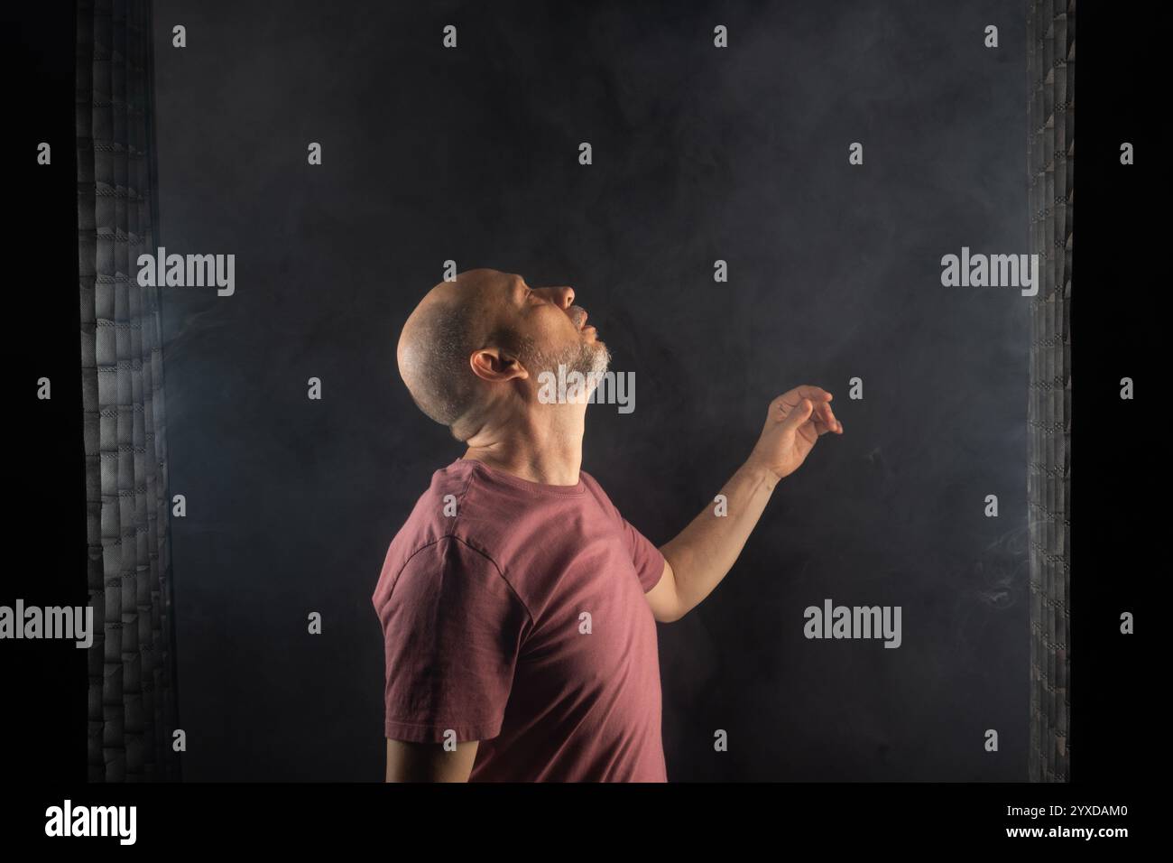 Bald and bearded man posing for photo in studio with dark smoky ...