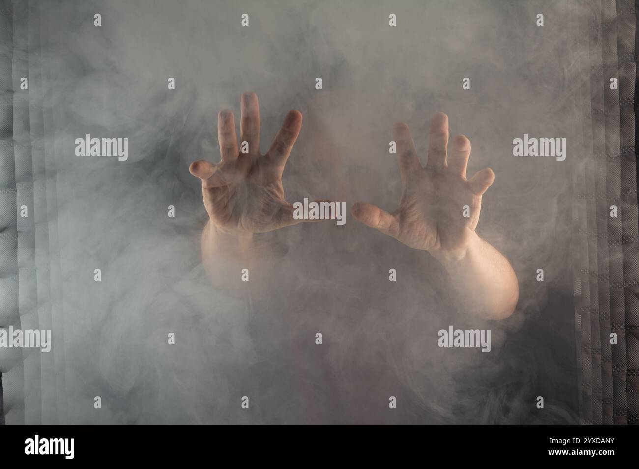 Hands of a white man appearing through thick smoke. Studio portrait ...