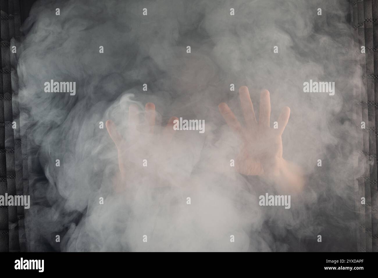 Hands of a white man appearing through thick smoke. Studio portrait ...