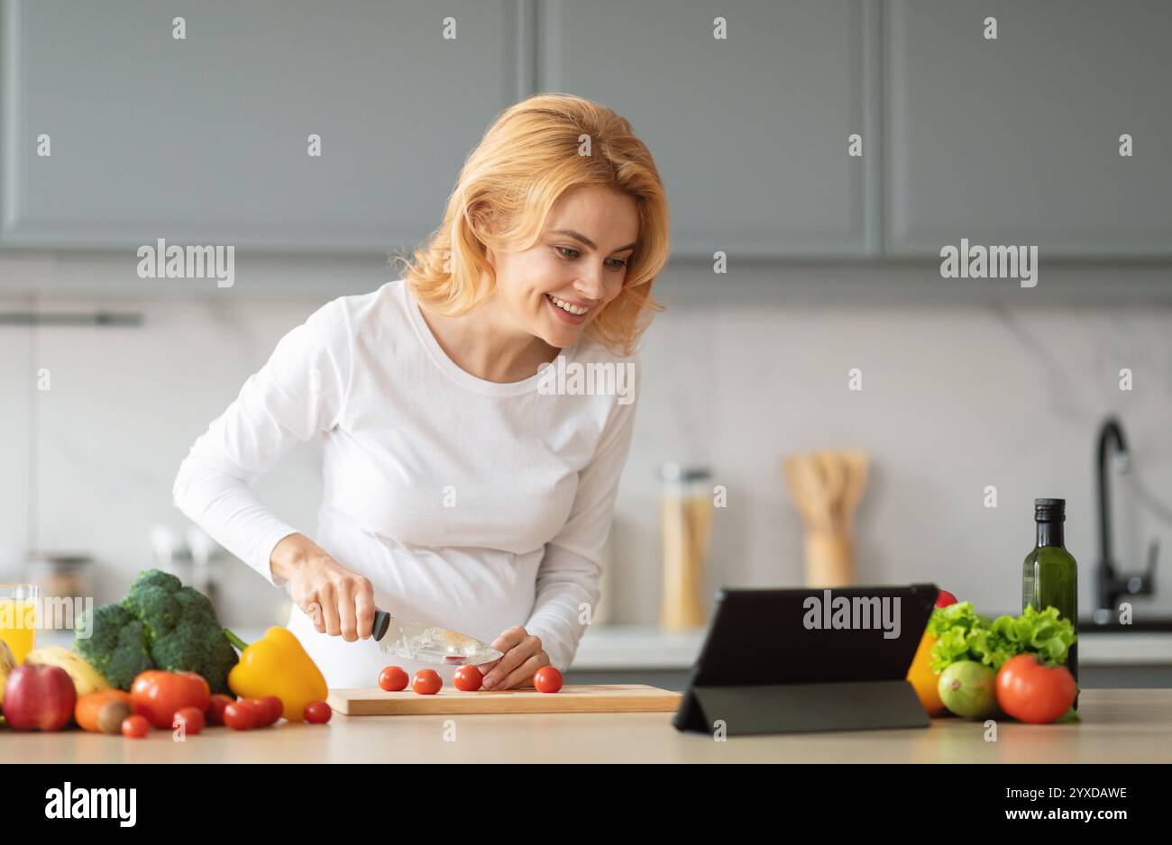 Woman cooking in a modern kitchen while following a recipe on a tablet ...