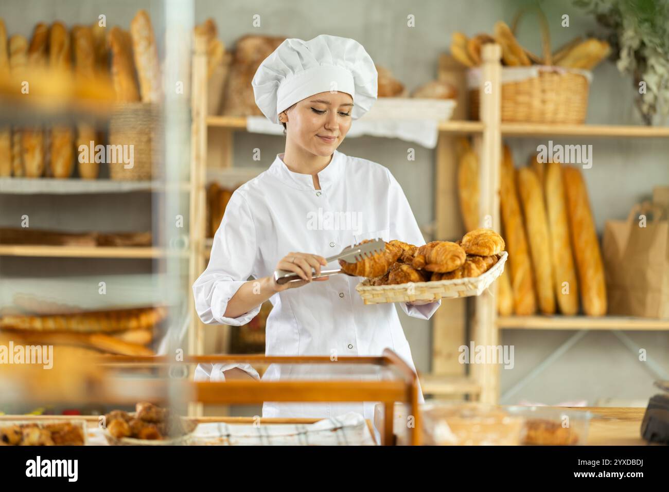 Young woman employee puts croissants in window, arranges display of ...
