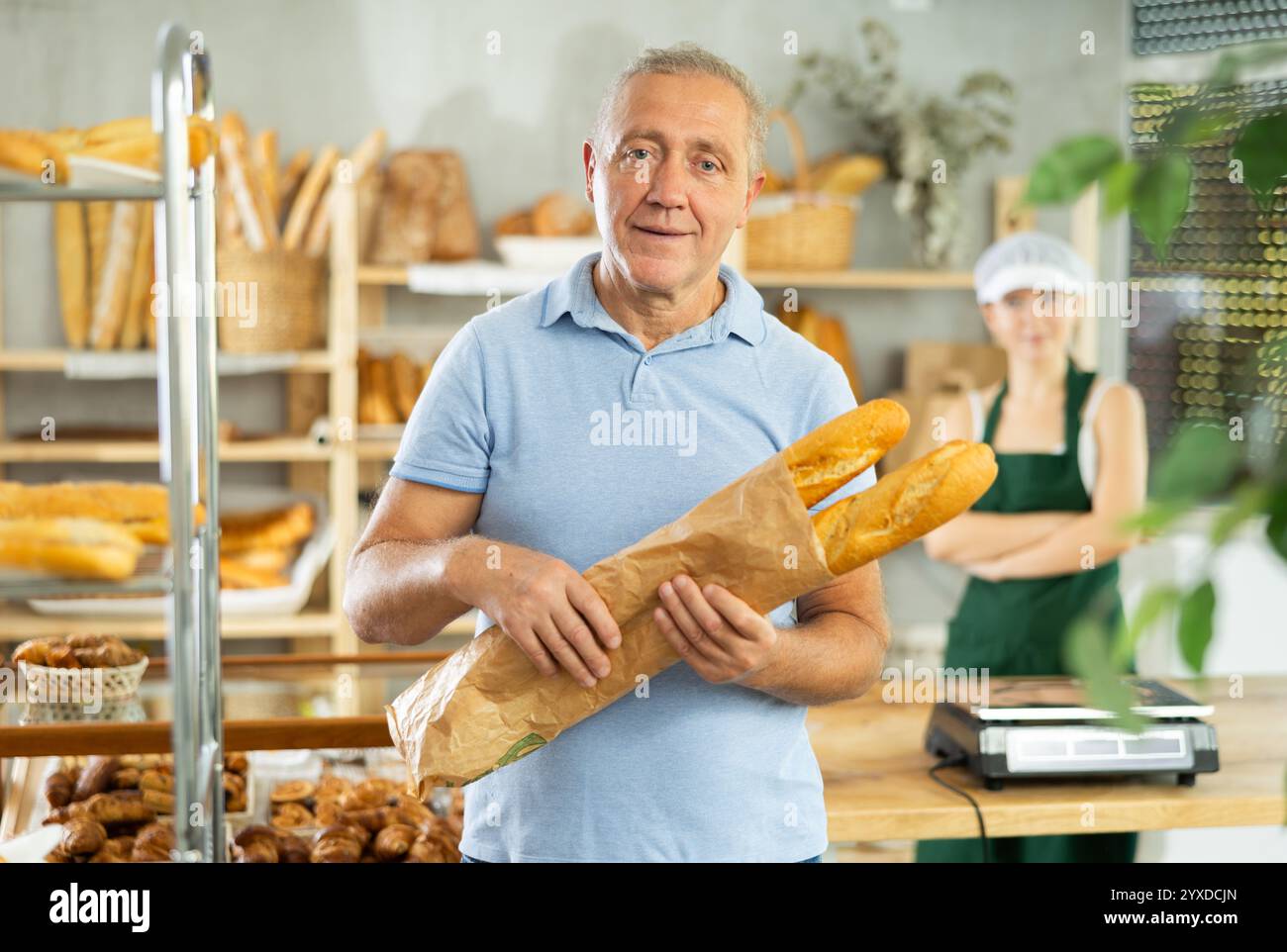 European aged male buyer stands proudly in front of fresh bread holding ...