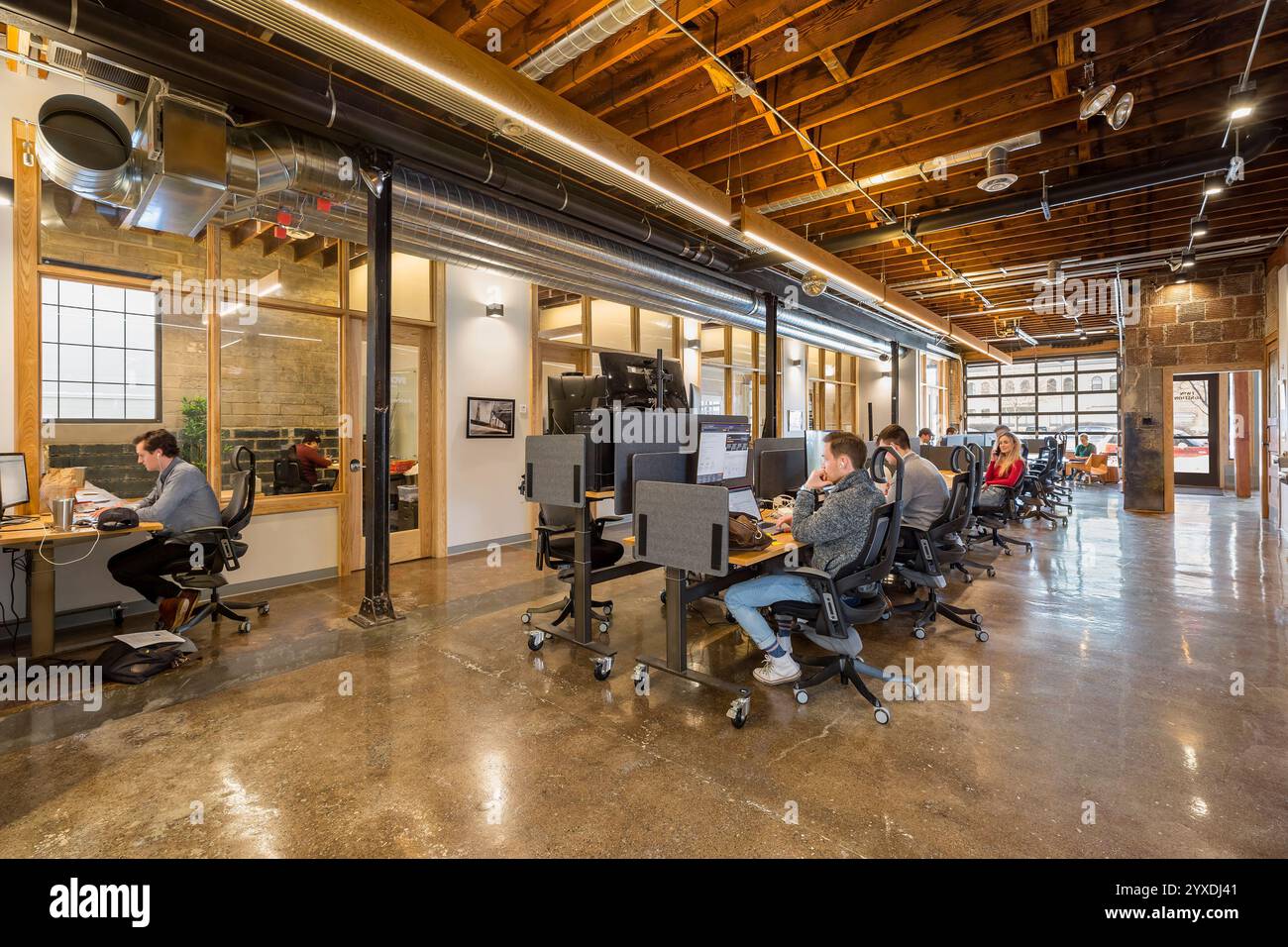 Tech entrepeneurs working at a long series of modular desks in tech ...