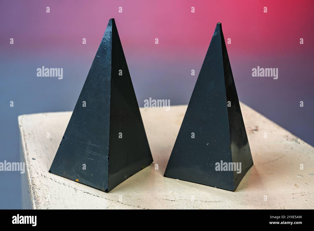 Two black pyramids are placed on a textured wooden surface. The ...