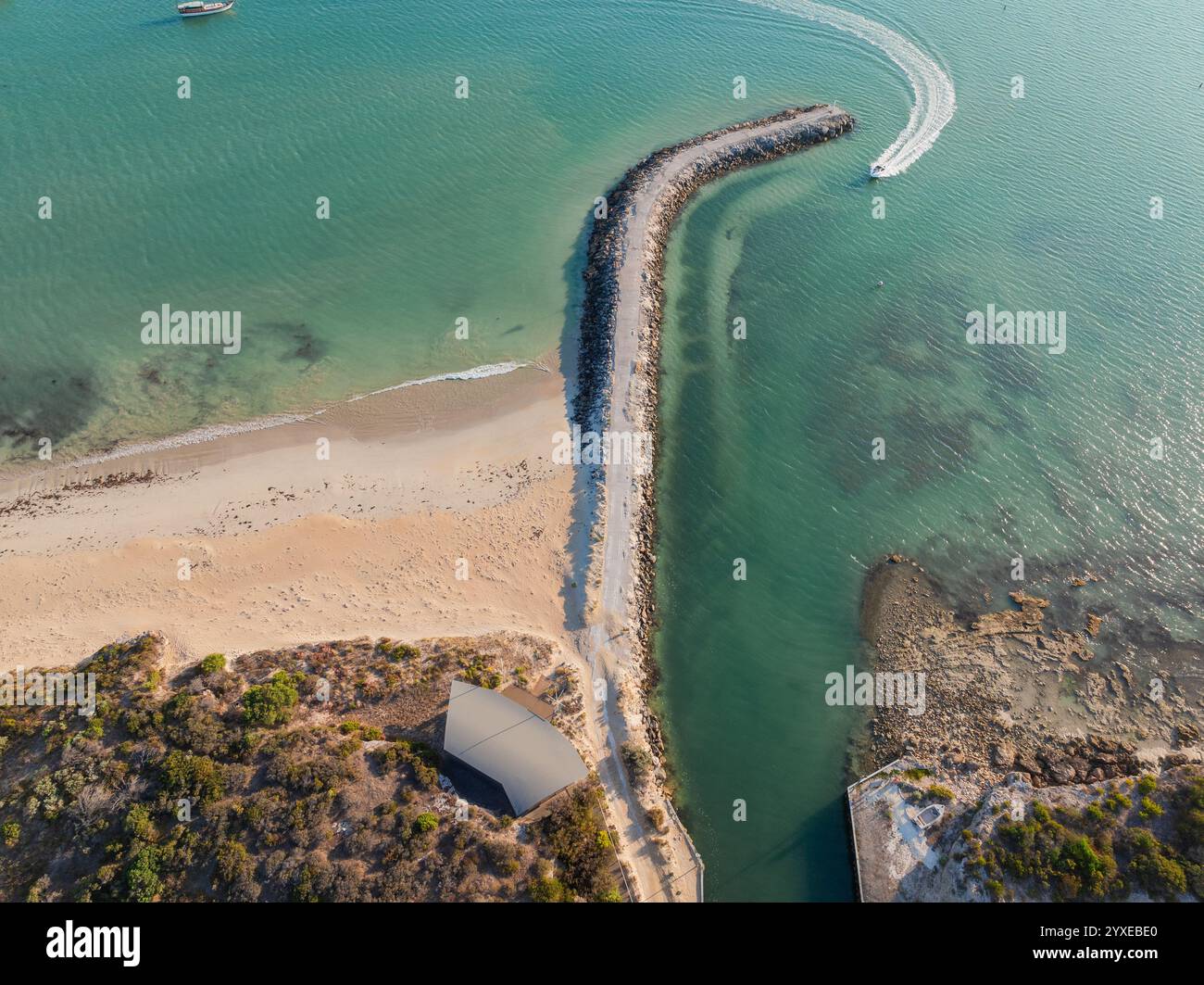 Aerial view of a small boat passing a curved breakwater alongside a ...