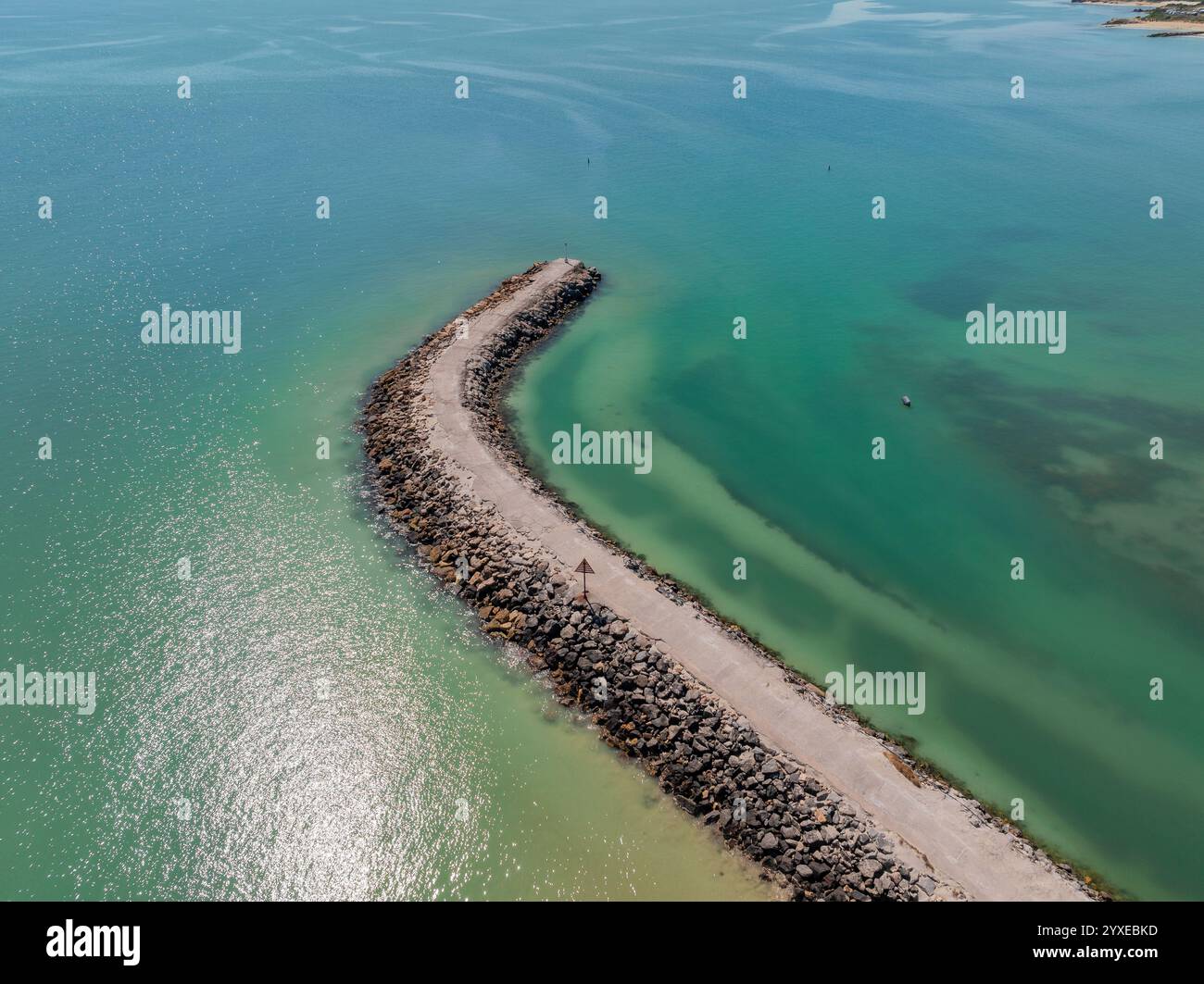 Aerial view of a curved rocky breakwater leading ot to sea at Robe on ...